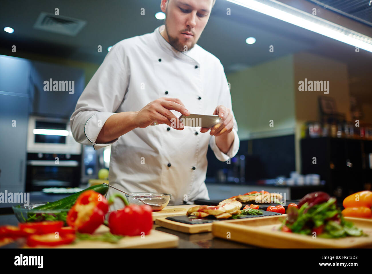 Young chief photographing what he cooked Stock Photo - Alamy