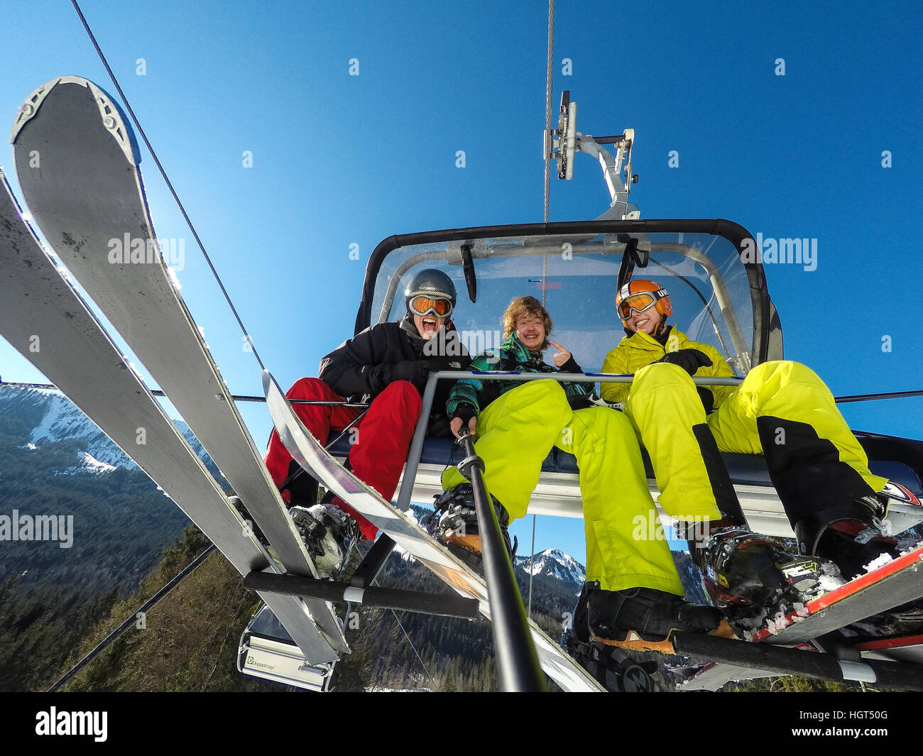Three teenagers on chairlift with skis and snowboard, taking selfie ...