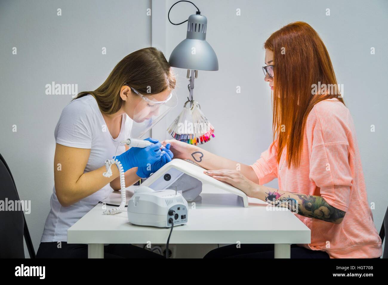 Hardware manicure in a salon. Manicurist is applying electric nail file ...