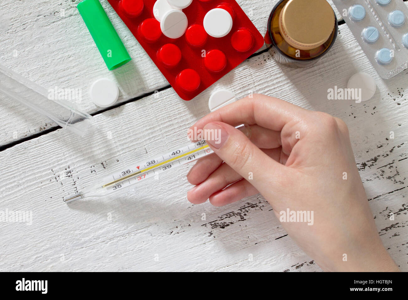 Thermometer in a female hand and various medications on a white wooden ...