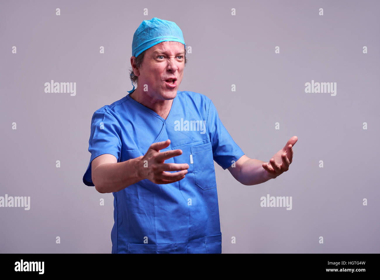 An angry middle aged male doctor standing in a blue scrubs and ...