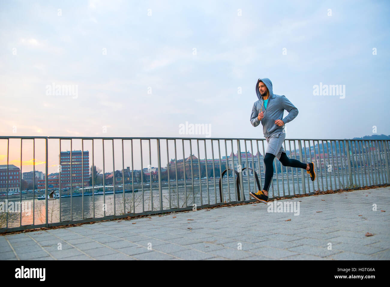 A handsome young man running in the sunset next to a fence on the ...