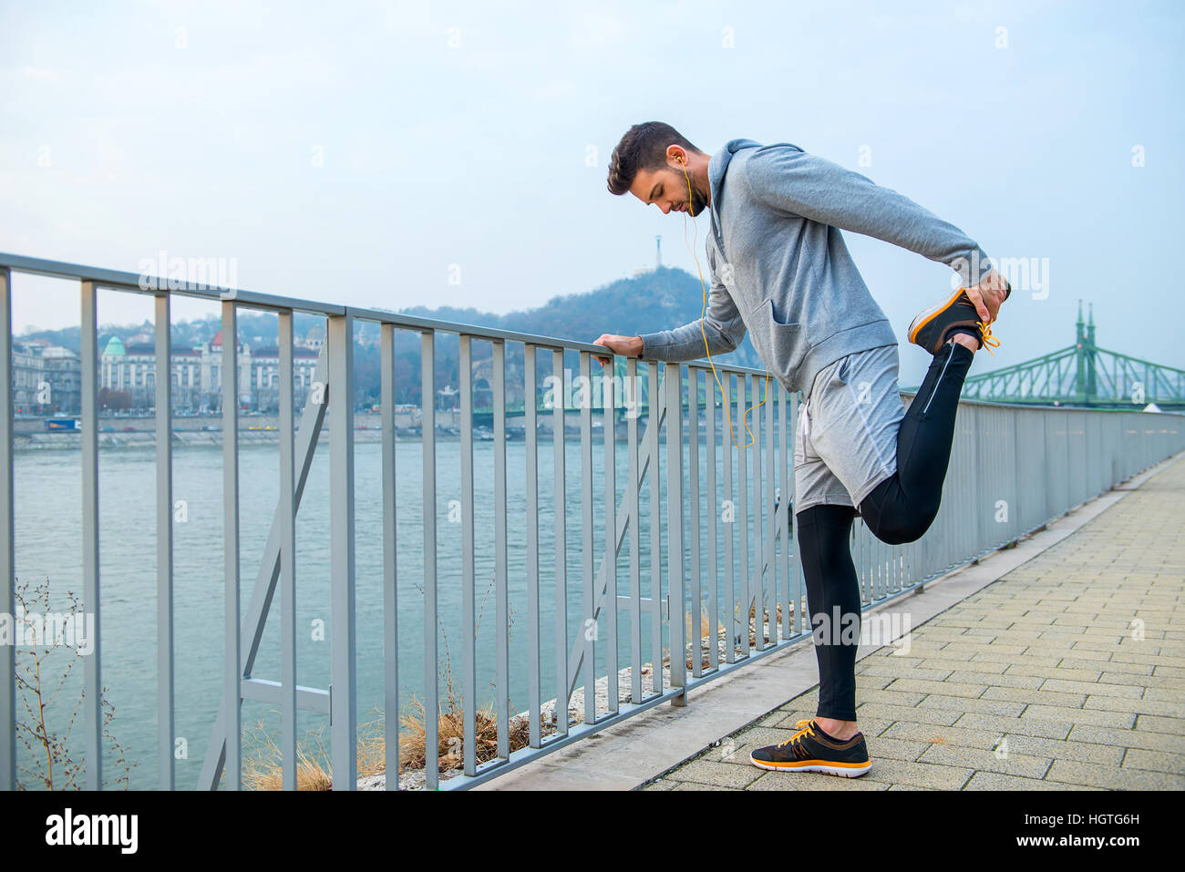 A handsome young man holding the fence and stretching his leg at the ...