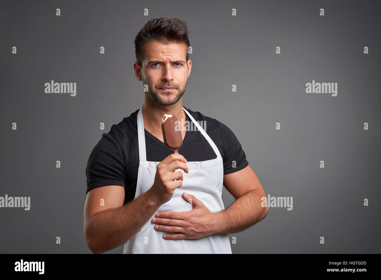 A handsome young barista man having a stomach ache while eating an ice ...
