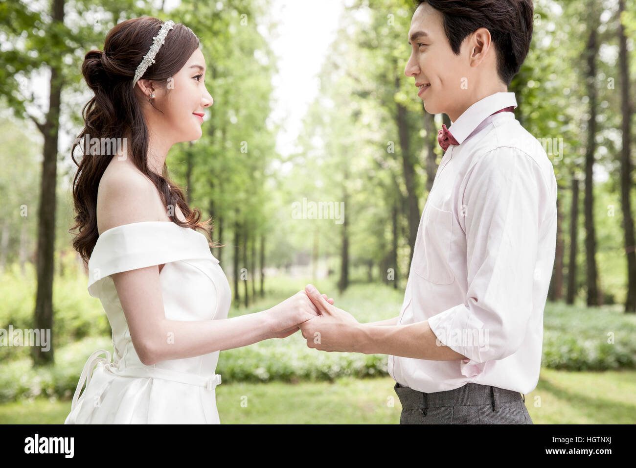 Side view of young smiling wedding couple holding hands face to face ...