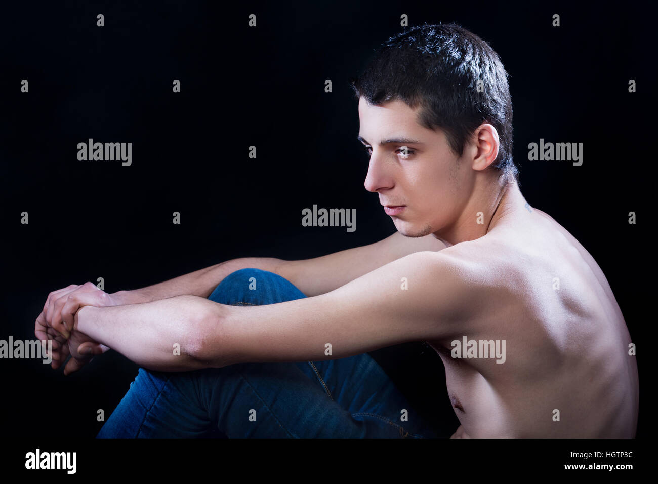 young man sitting down depressed against black Stock Photo - Alamy