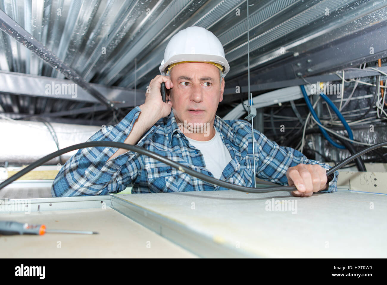 Contractor in roof space, talking on telephone Stock Photo - Alamy