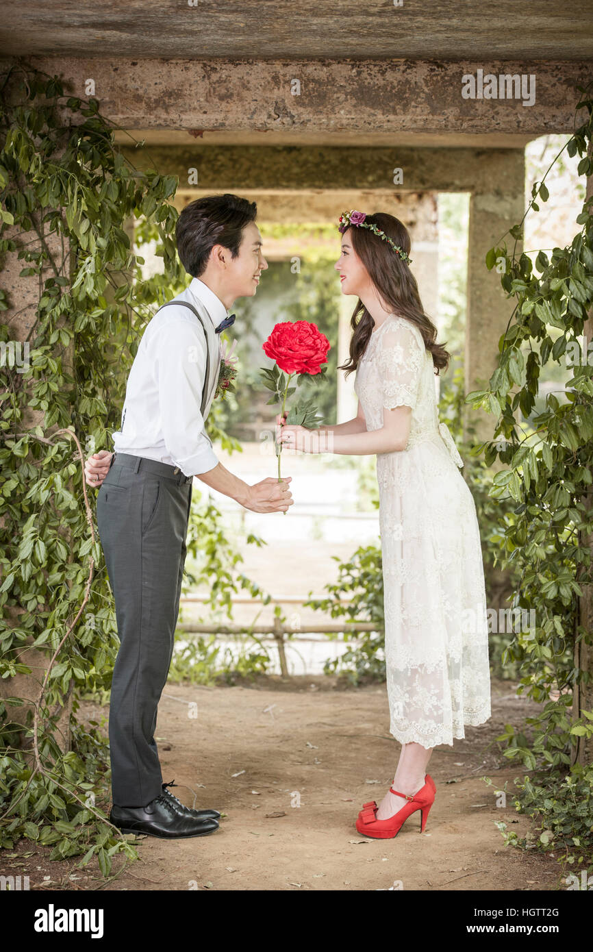 Side view of young wedding couple with flowers standing face to face ...