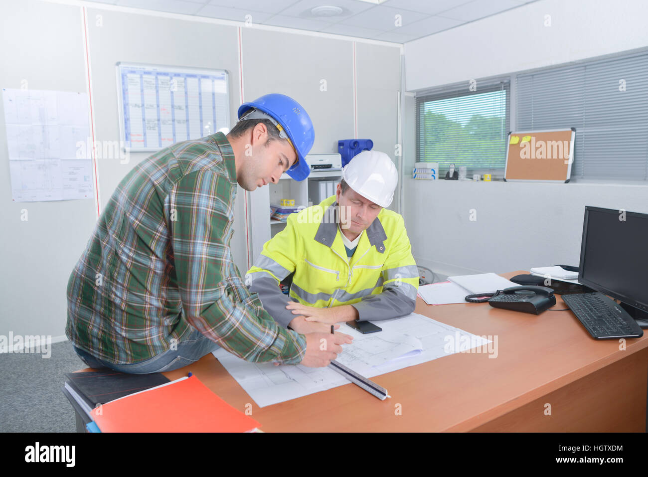 Two men working on scale drawings, one sat on table Stock Photo - Alamy