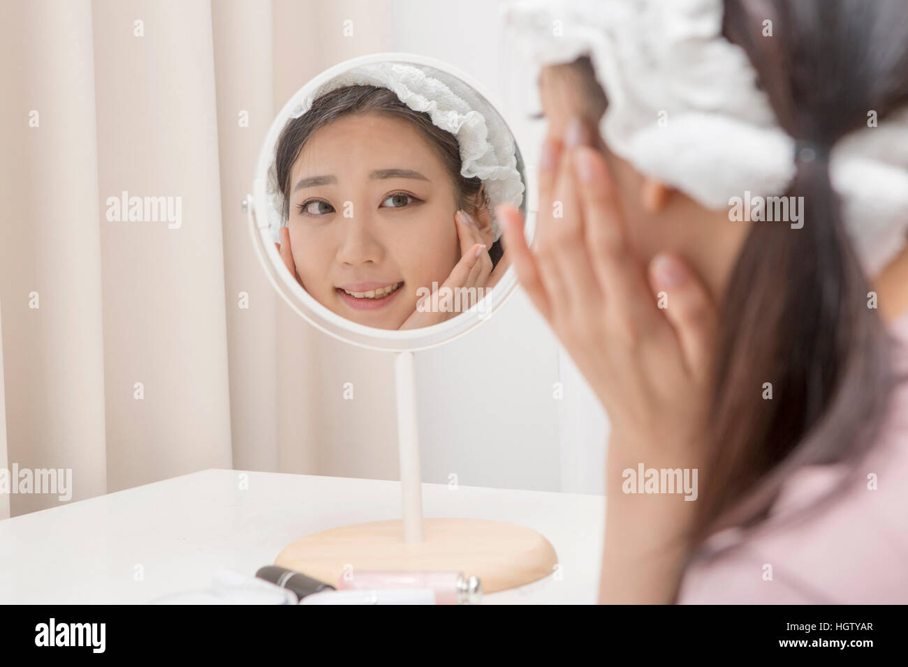 Portrait of young woman touching her cheeks looking in mirror Stock ...