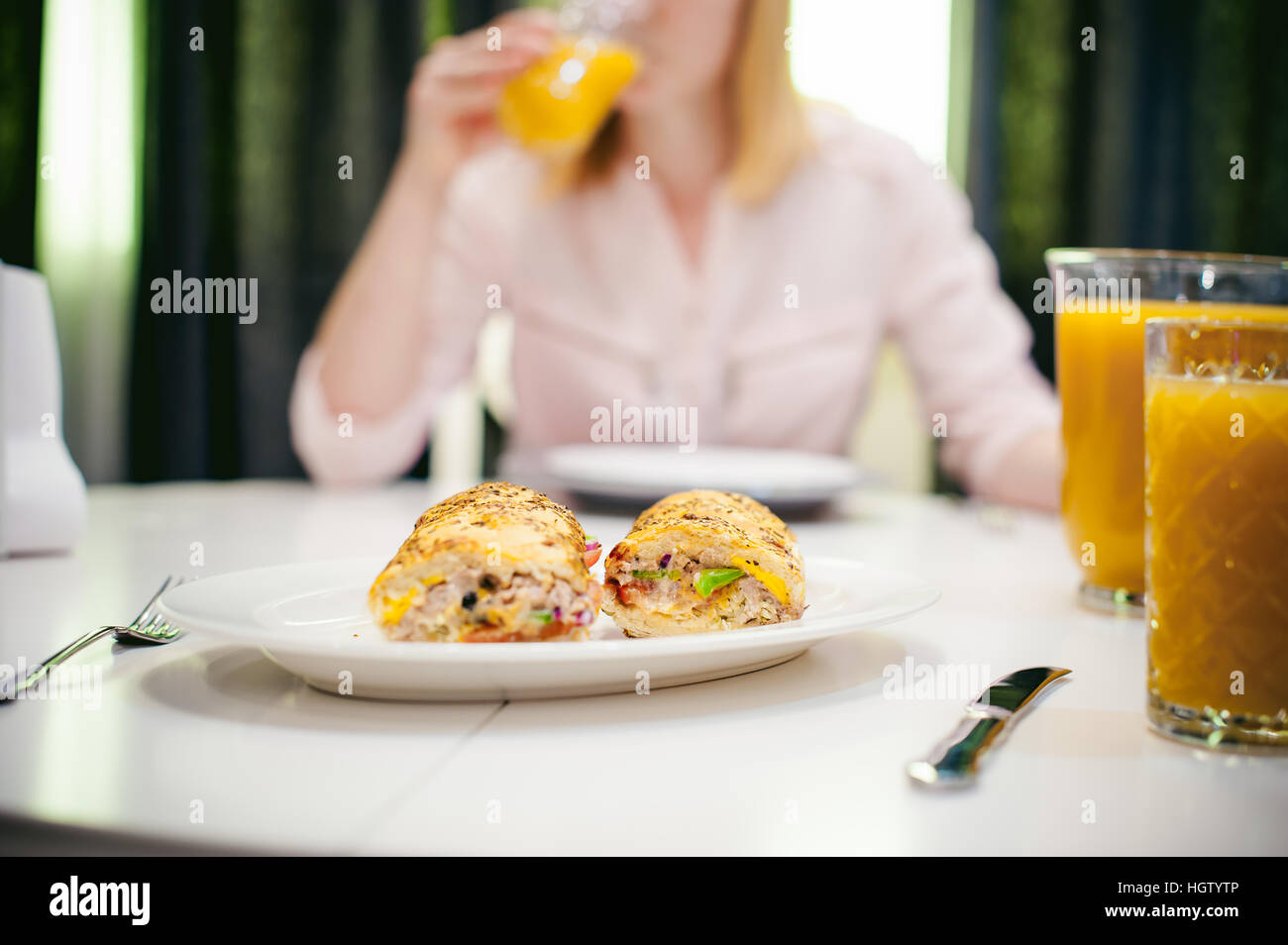 Pretty blonde woman in a pink shirt, eating at home. breakfast sandwich ...