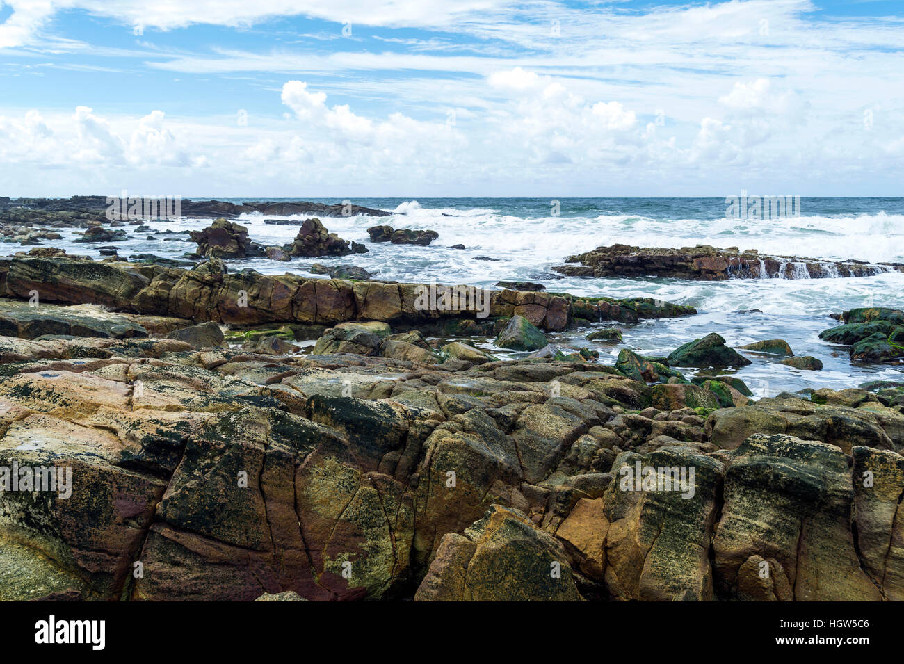 Waves wash over tidal pools and rock slabs on a rugged coastline Stock ...