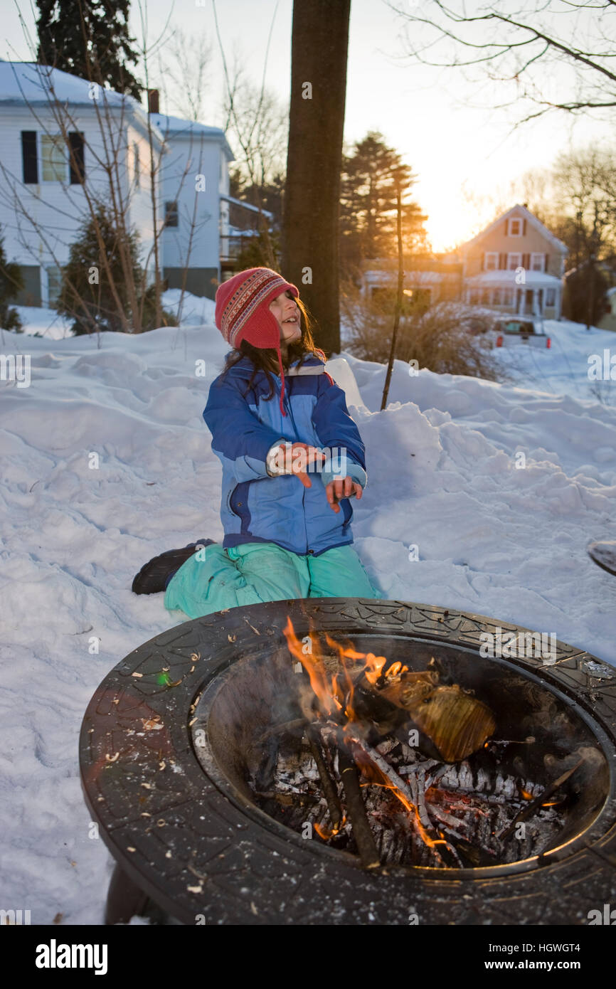 A girl (age 8) warms her hands over a fire pit in a backyard in ...