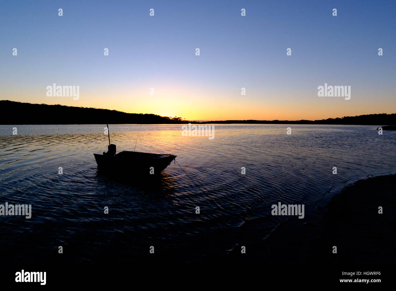 Small boat in silhouette anchored near water's edge at sunrise on a ...