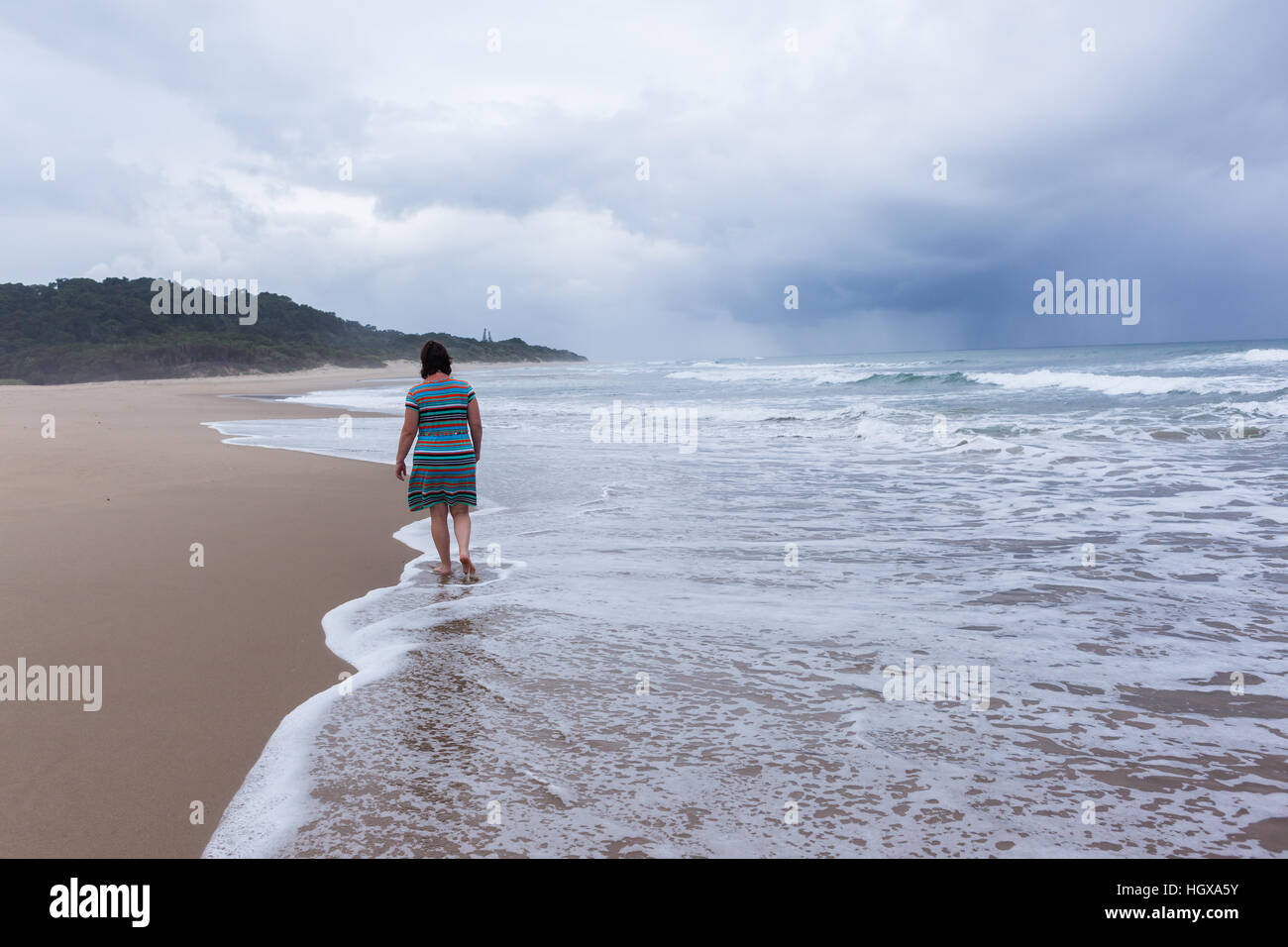 Woman walking remote beach ocean coastline with coming rain storm ...