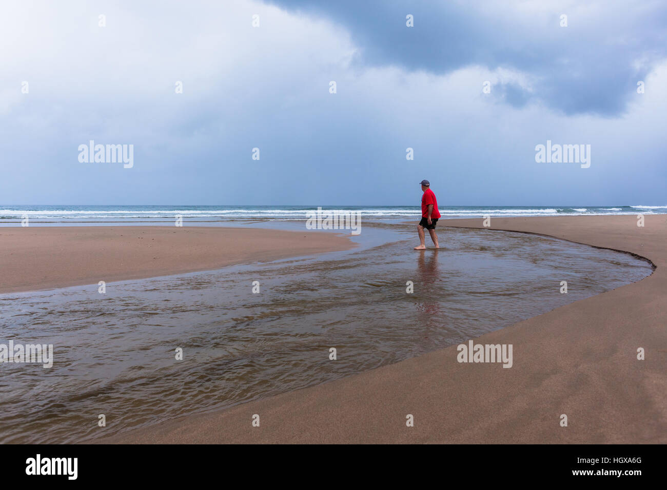 Man walking remote beach ocean coastline with coming rain storm clouds ...