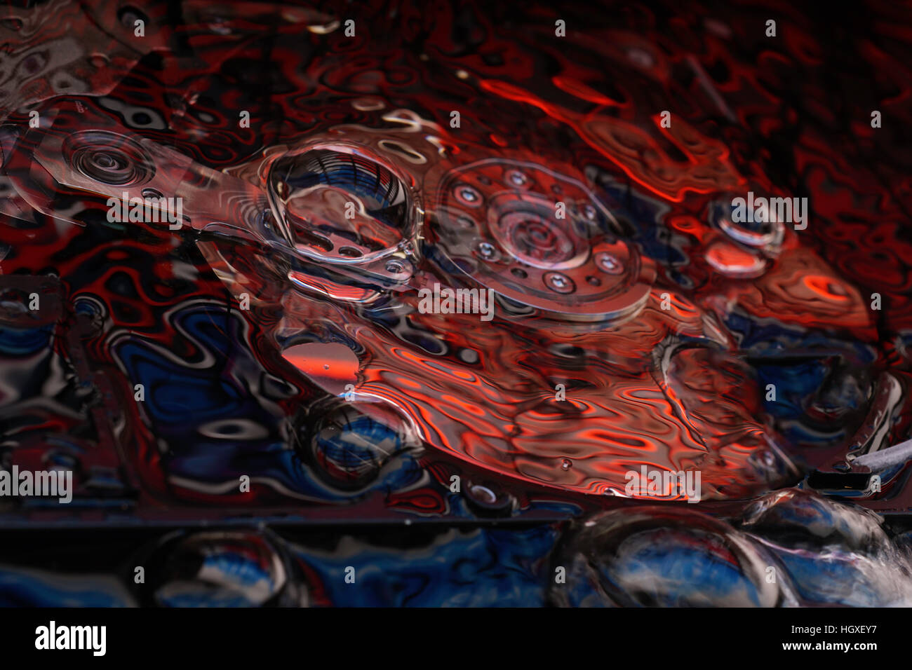 Opened Computer hard disk drive in studio with bubbles and dark red and ...