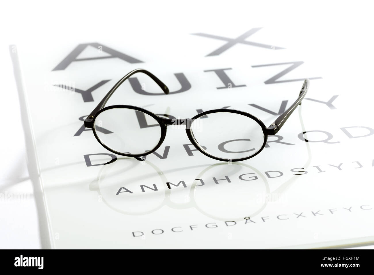 Black oval glasses laying over white glossy eye chart table, sight test ...