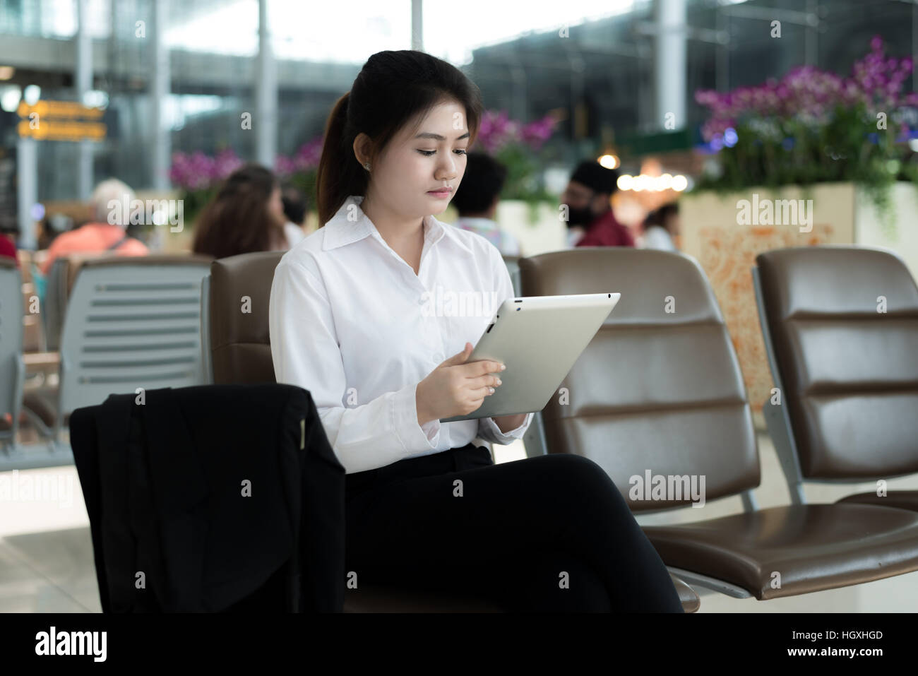 Asian young woman passenger at airport, using her tablet computer while ...