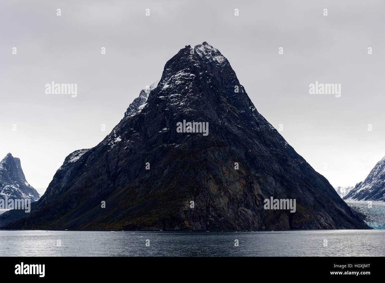 A cone-shaped mountain rises from the dark waters of an Arctic fjord ...