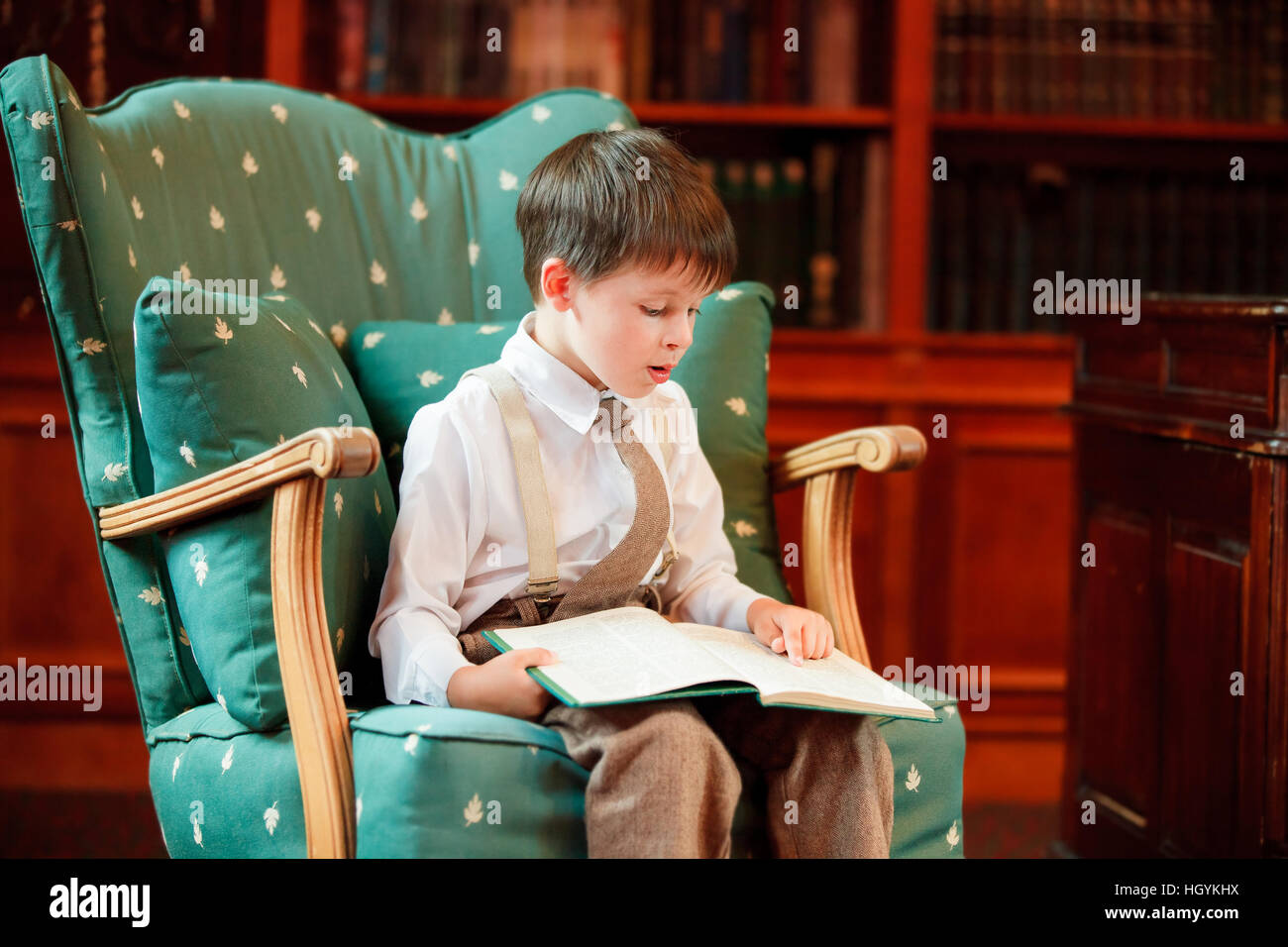 Cute little boy reading book on armchair Stock Photo - Alamy