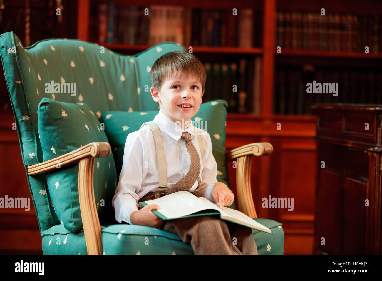 Cute little boy reading book on armchair Stock Photo - Alamy