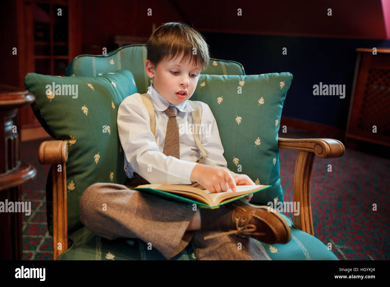 Cute little boy reading book on armchair Stock Photo - Alamy