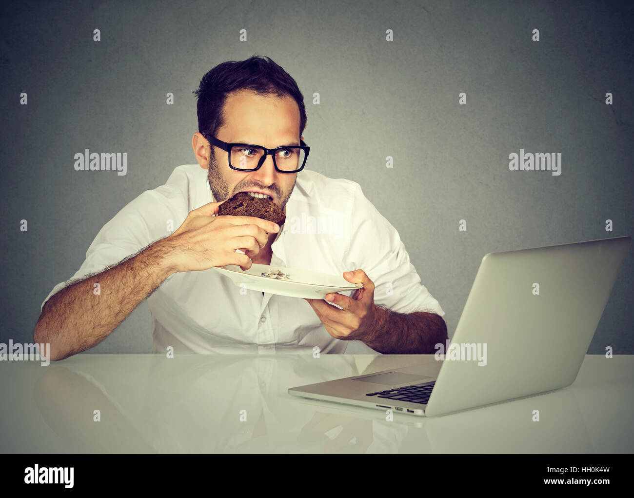Young student man eating while working on laptop Stock Photo - Alamy