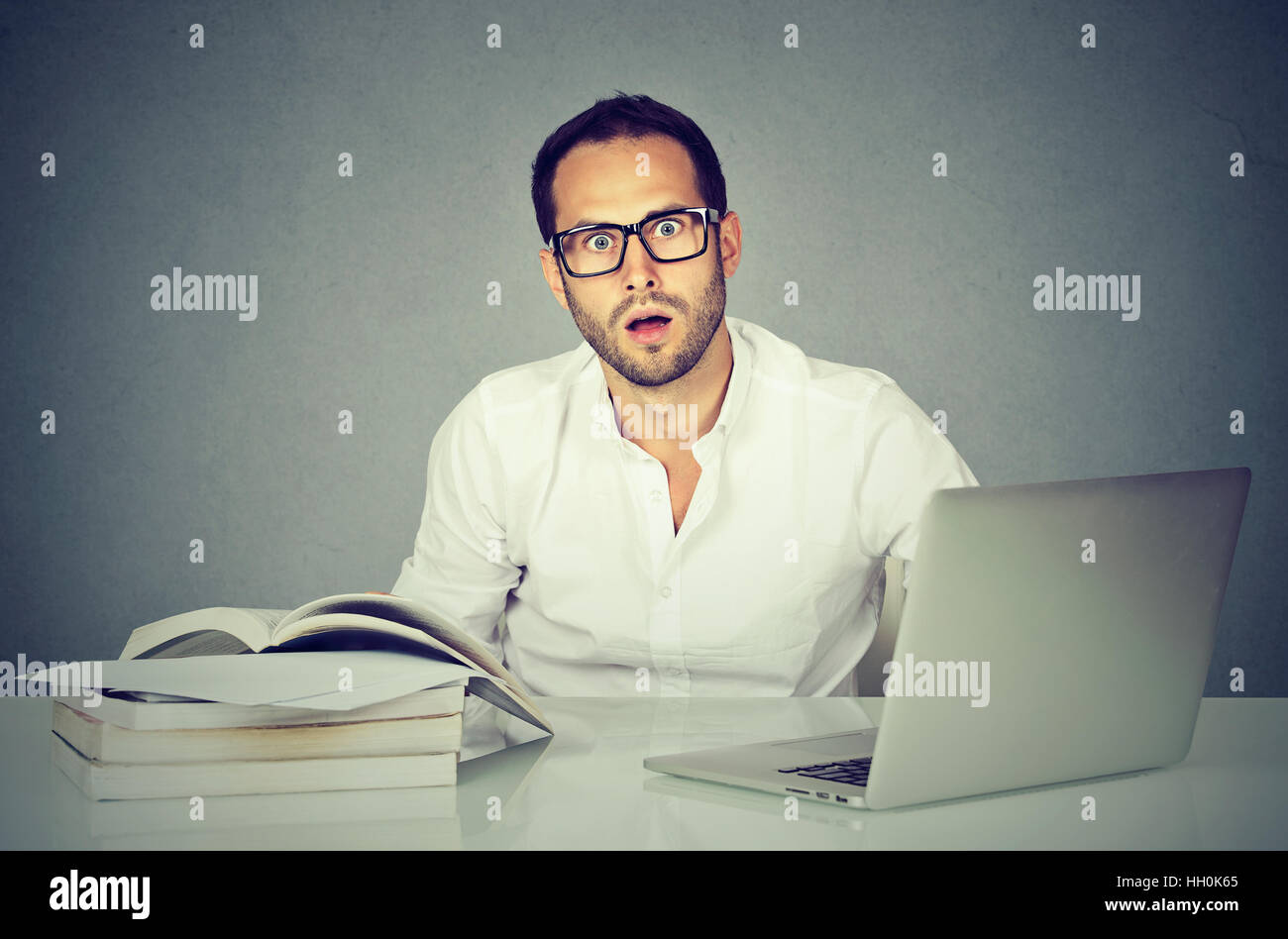 Surprised confused man sitting studying at table with stack of books ...