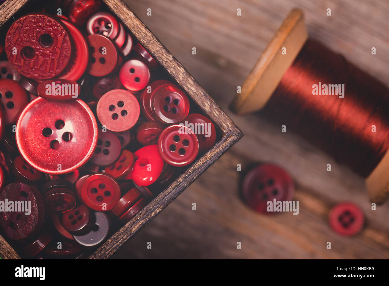 A close up of a box of red buttons, with a spool of red thread ...
