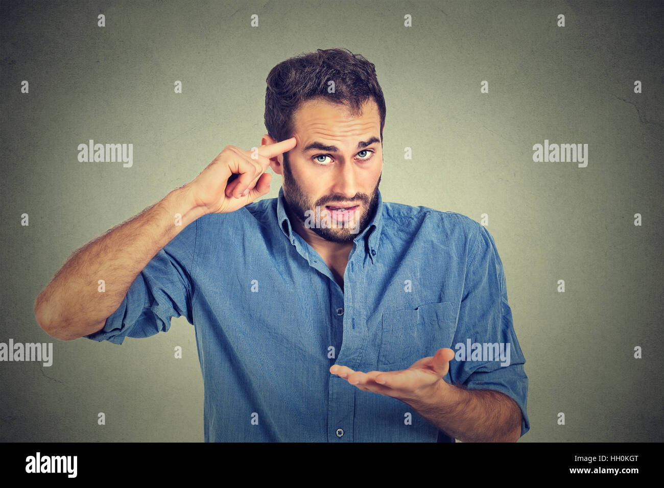 angry mad young man gesturing with his finger against temple asking are ...