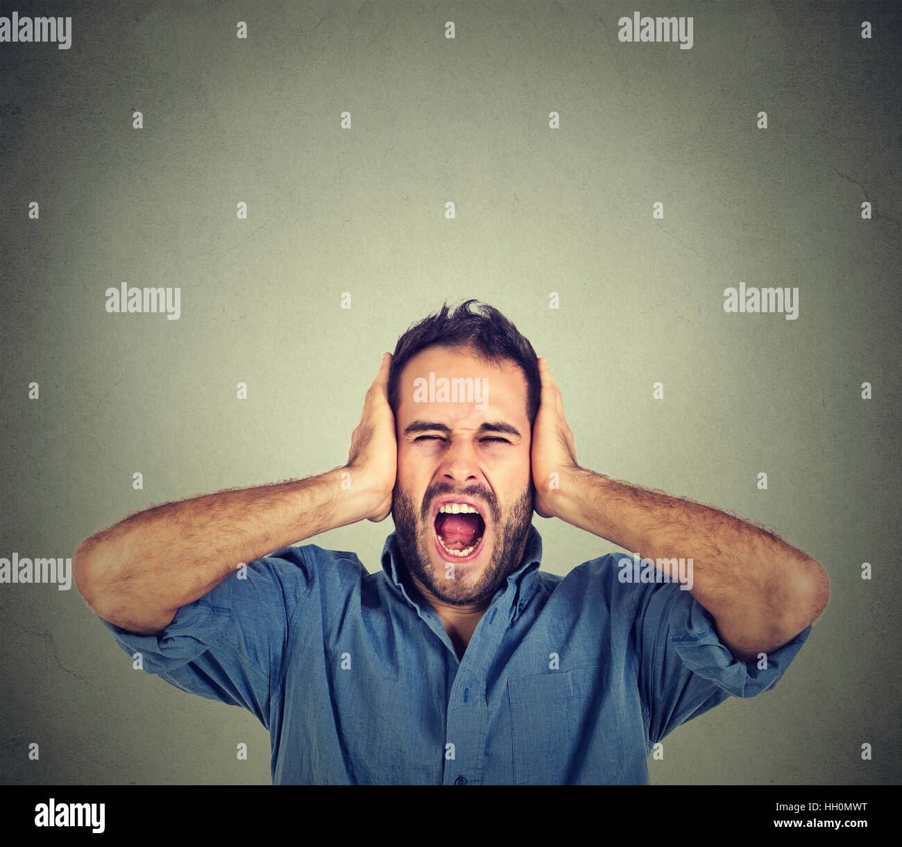 Portrait young man screaming mouth open, holding head with hands ...