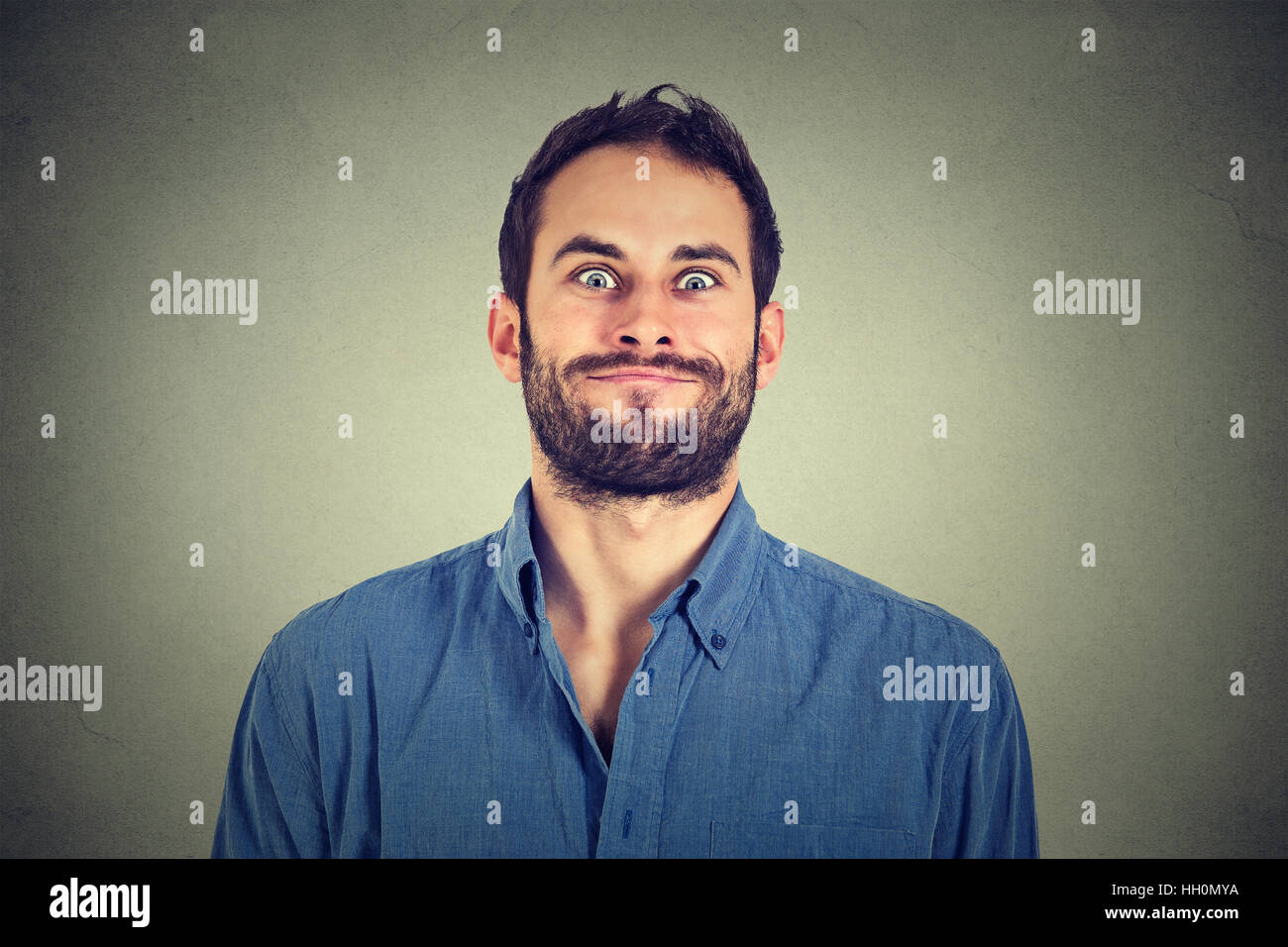 Crazy looking man making funny faces isolated on gray wall background ...