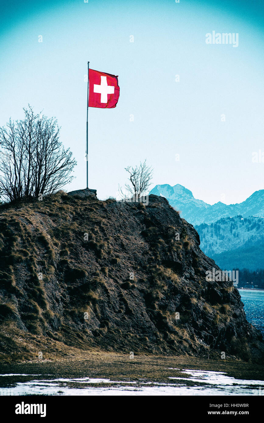 Swiss flag flying above a mountain in the alps covered in light winter ...