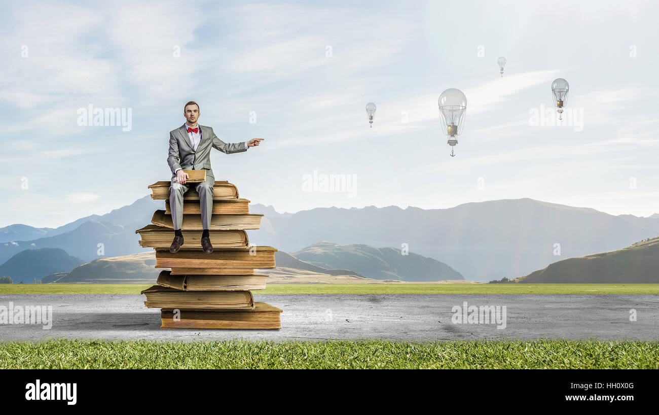 Young businessman sitting on pile of giant books Stock Photo - Alamy