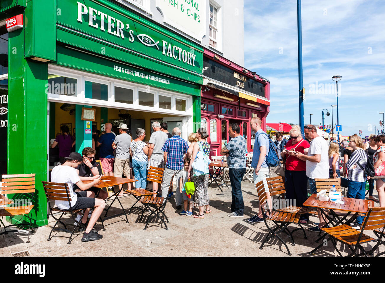 Long mid-day queue of people for fish and chip shop on seafront during ...