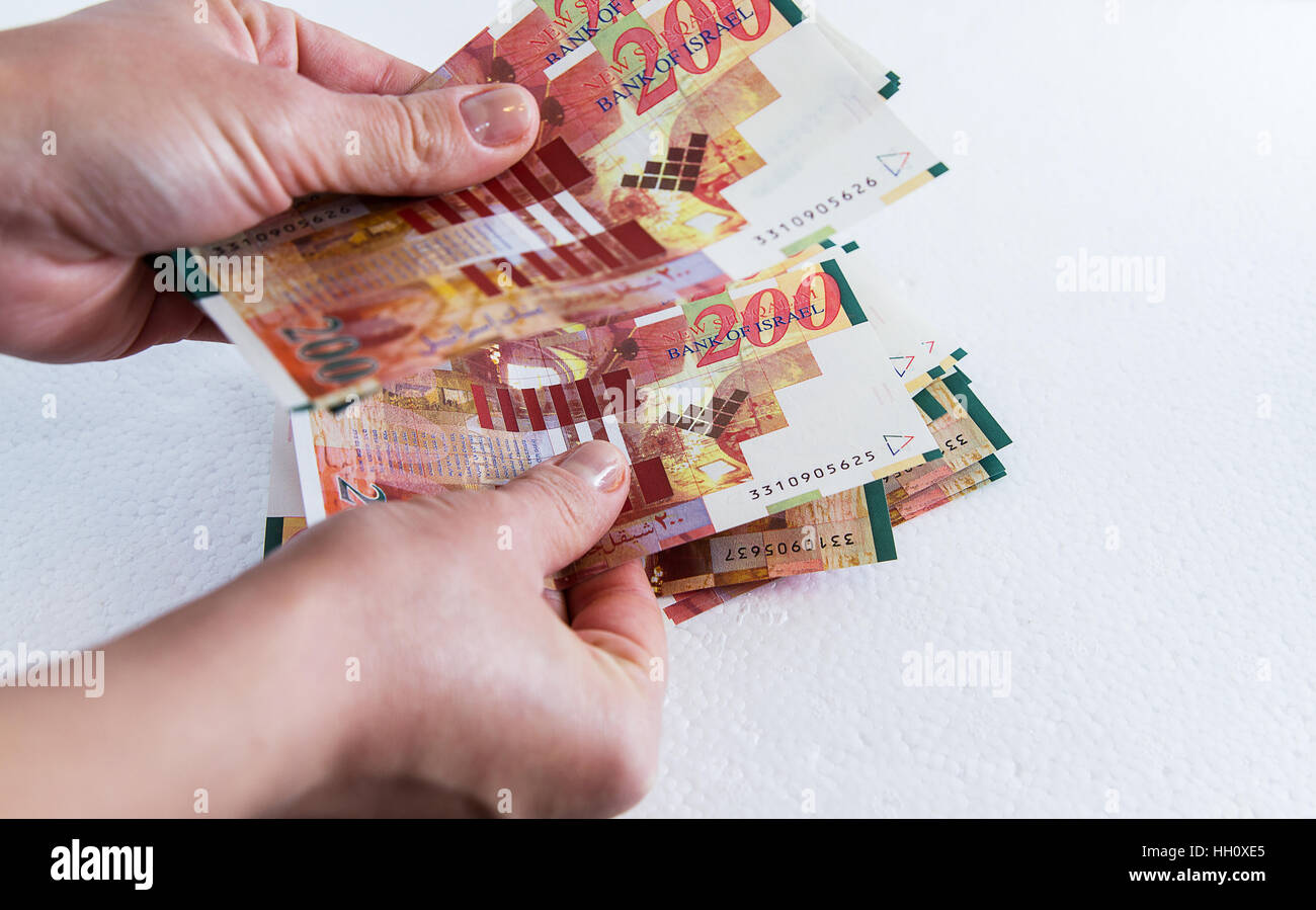 A female hand holding two hundred shekel bank notes against wood ...