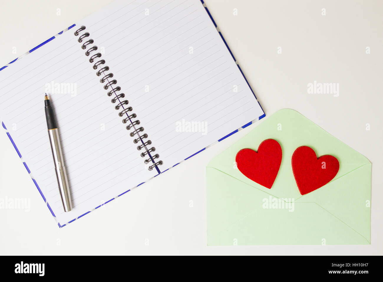 Open notebook, pen, pastel envelope and two red felt hearts on white ...