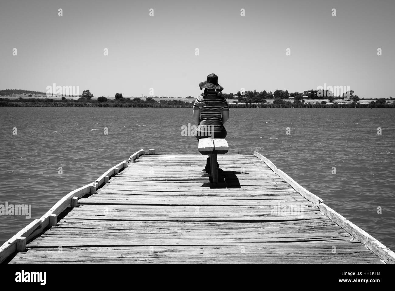 Woman sitting on pier looking out over the water Stock Photo - Alamy