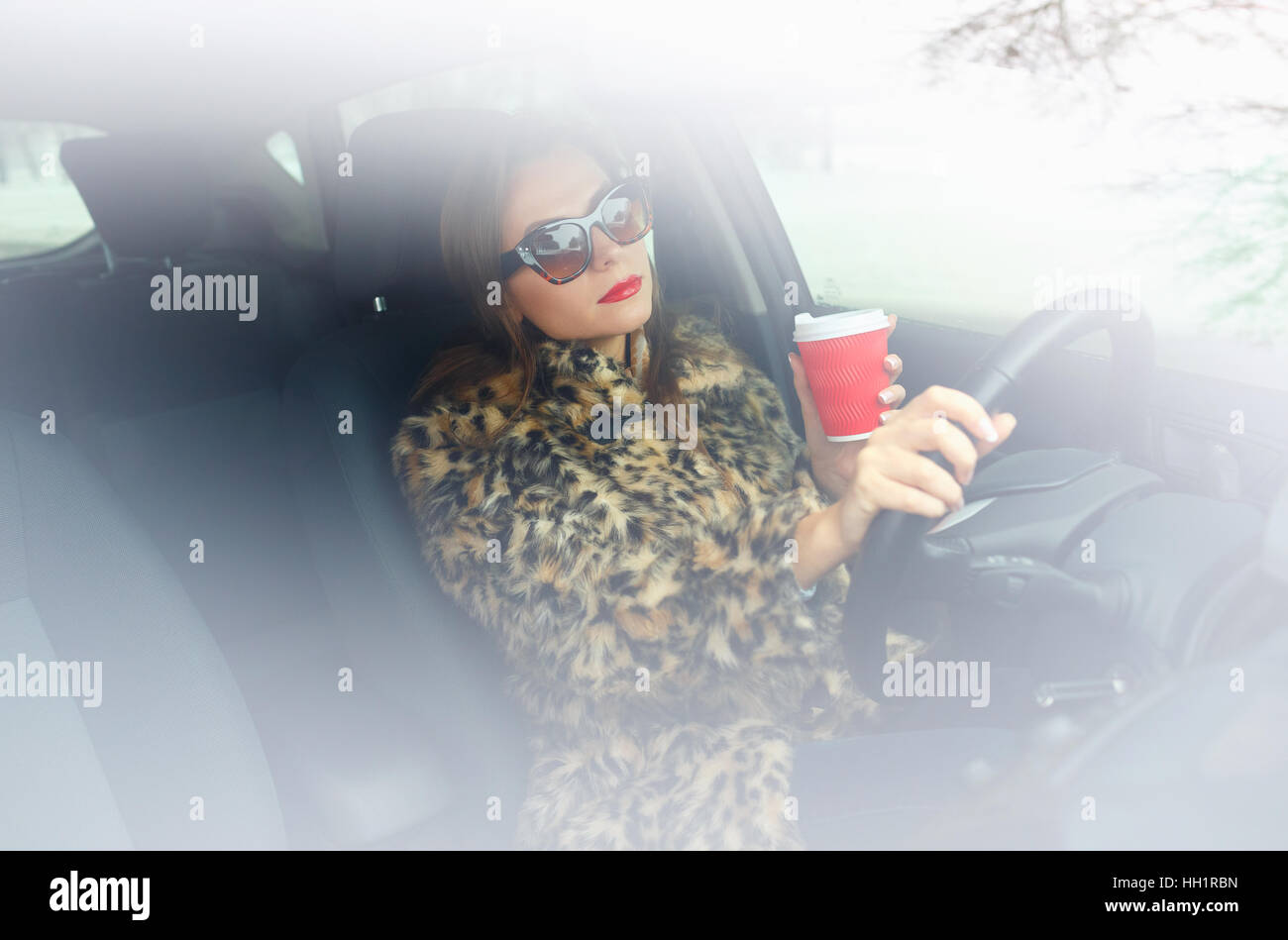 Beautiful woman in a fur coat with red lips with coffee to go driving ...