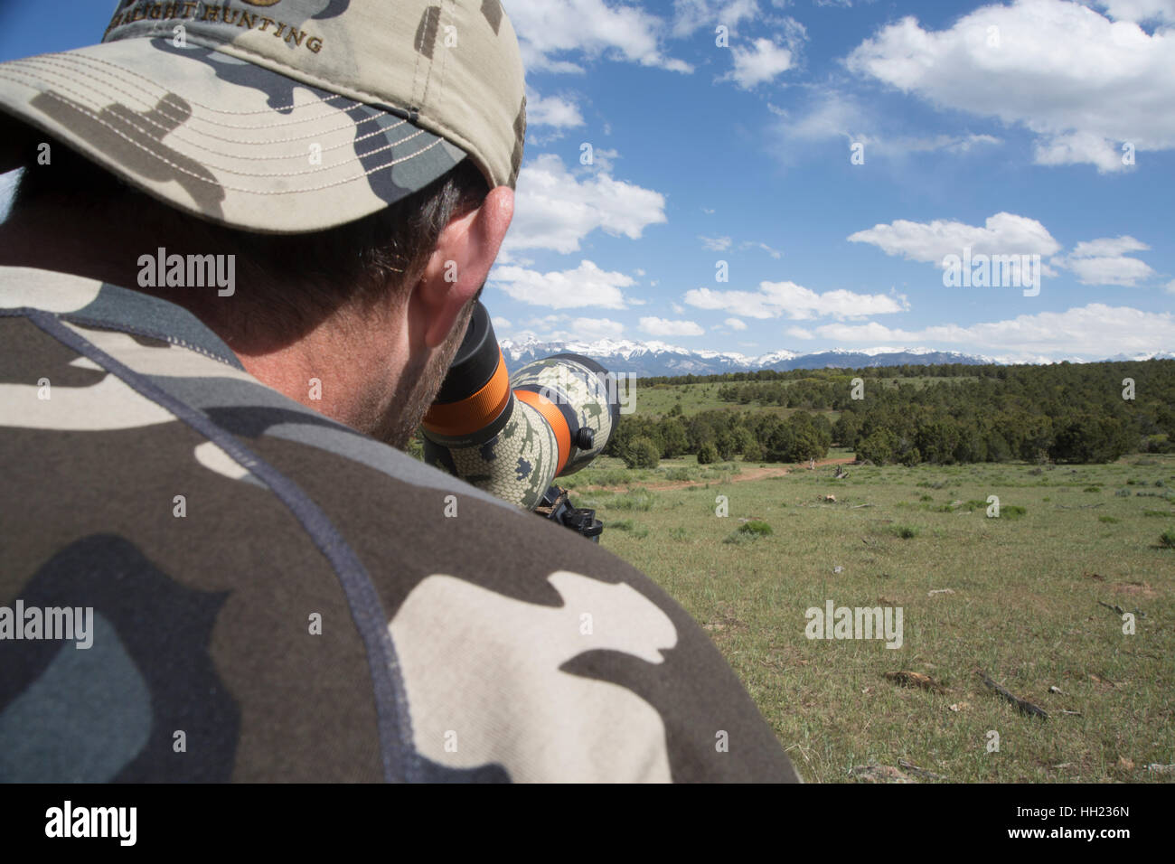 View from behind of a hunter looking through a spotting scope looking ...