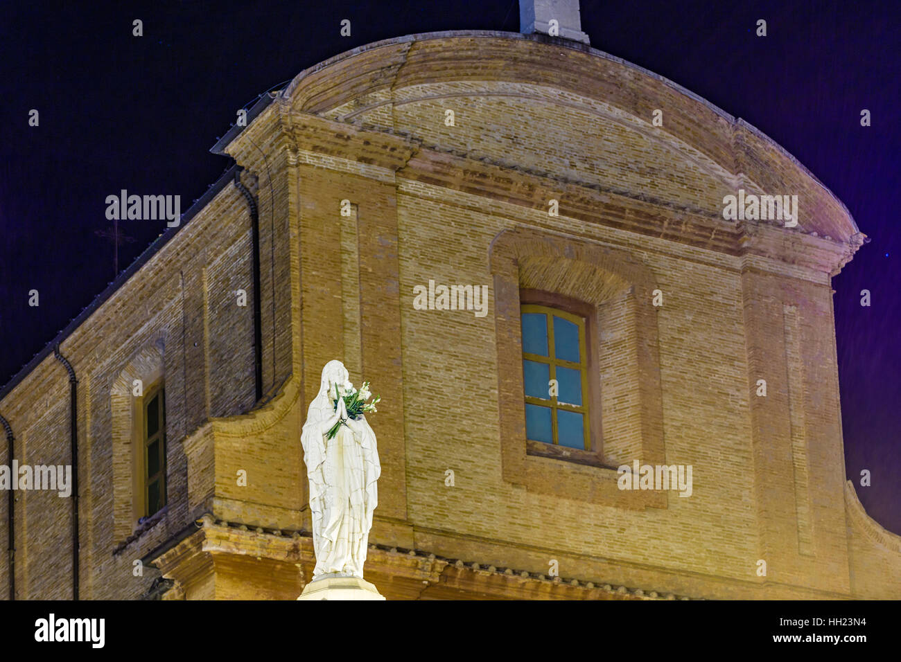 The statue of the Blessed Virgin Mary holding white roses at night ...