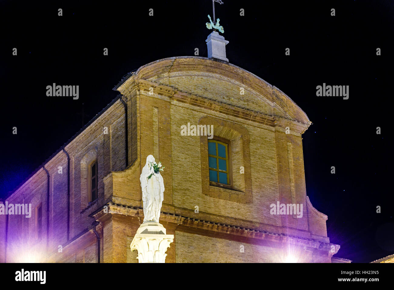The statue of the Blessed Virgin Mary holding white roses at night ...