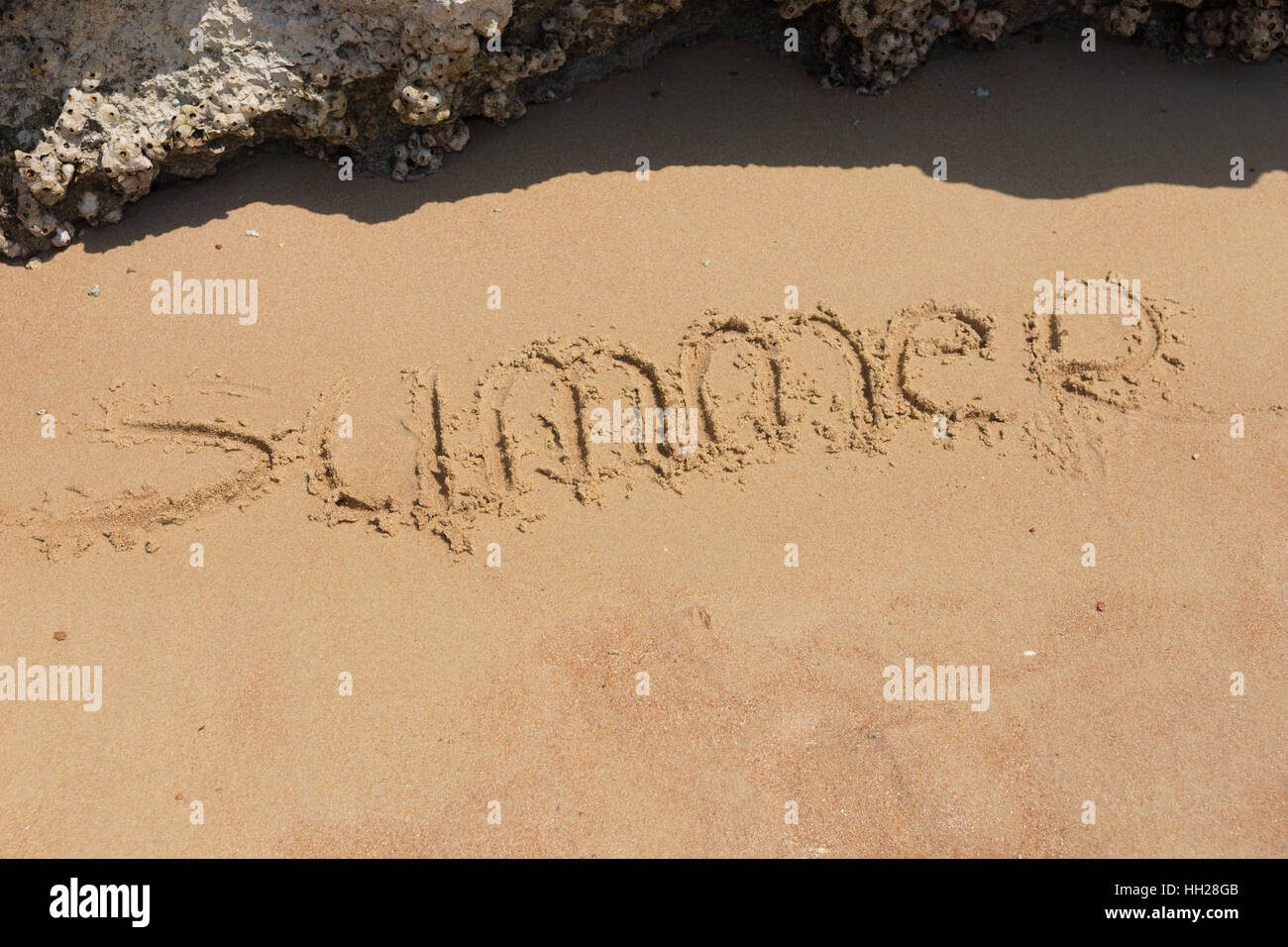 Hand made text in sand on a beach inscription summer under the rock on ...