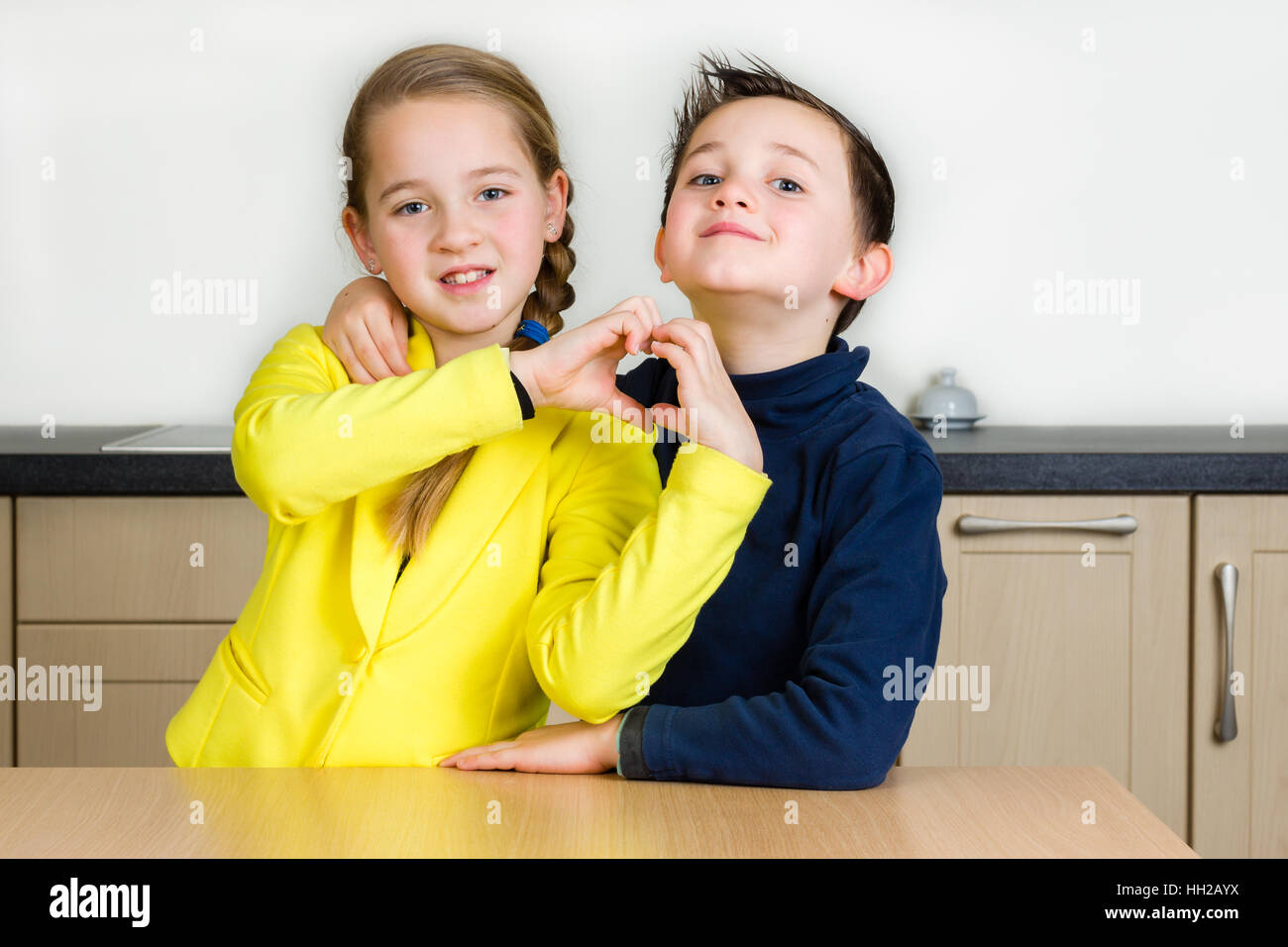 Kids (siblings boy and girl) hug and girl forms heart with hands at ...
