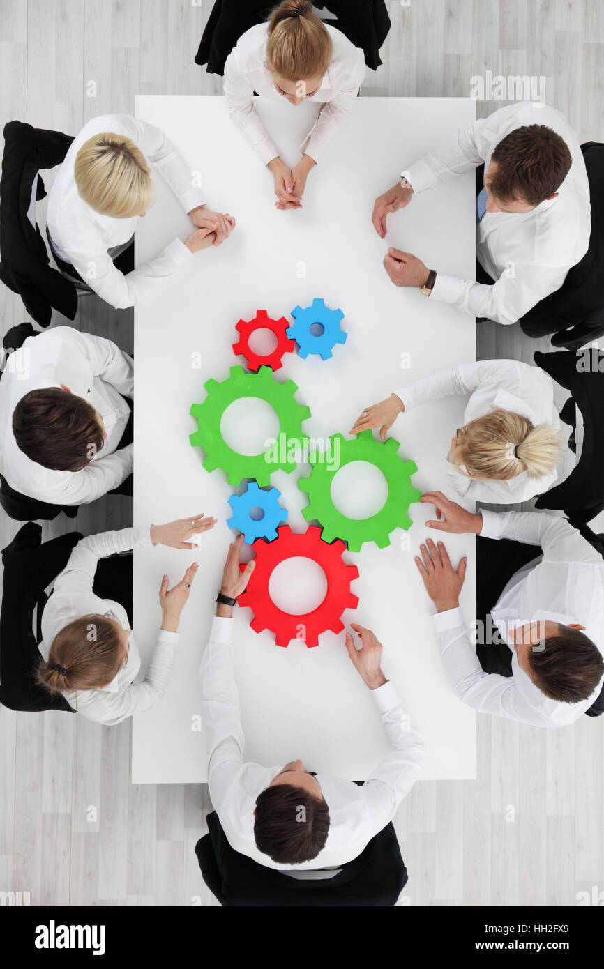 Business team sitting around the table with cogs, teamwork concept ...
