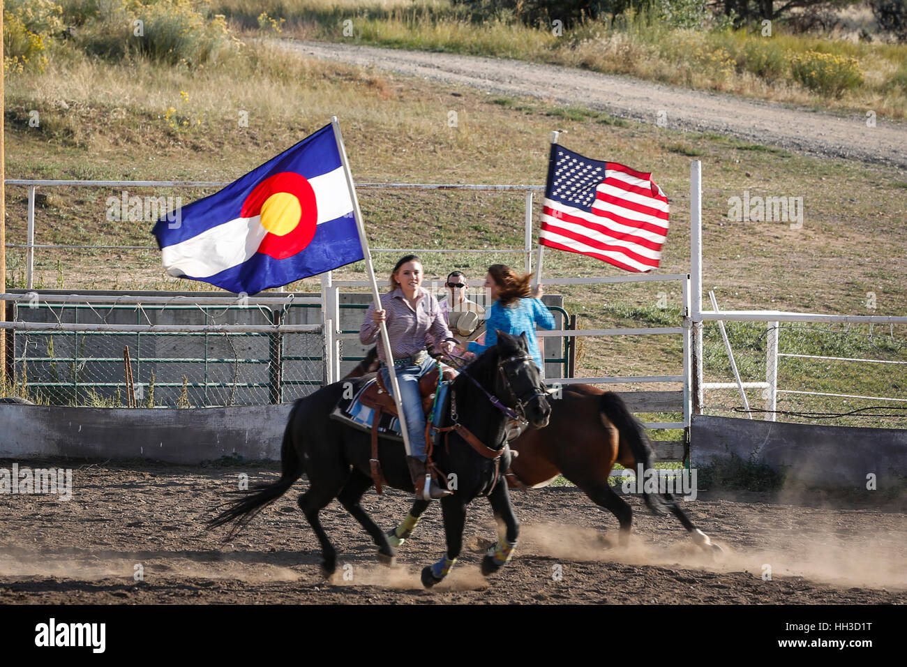 Two young women riding around a rodeo arena on horseback carrying flags ...