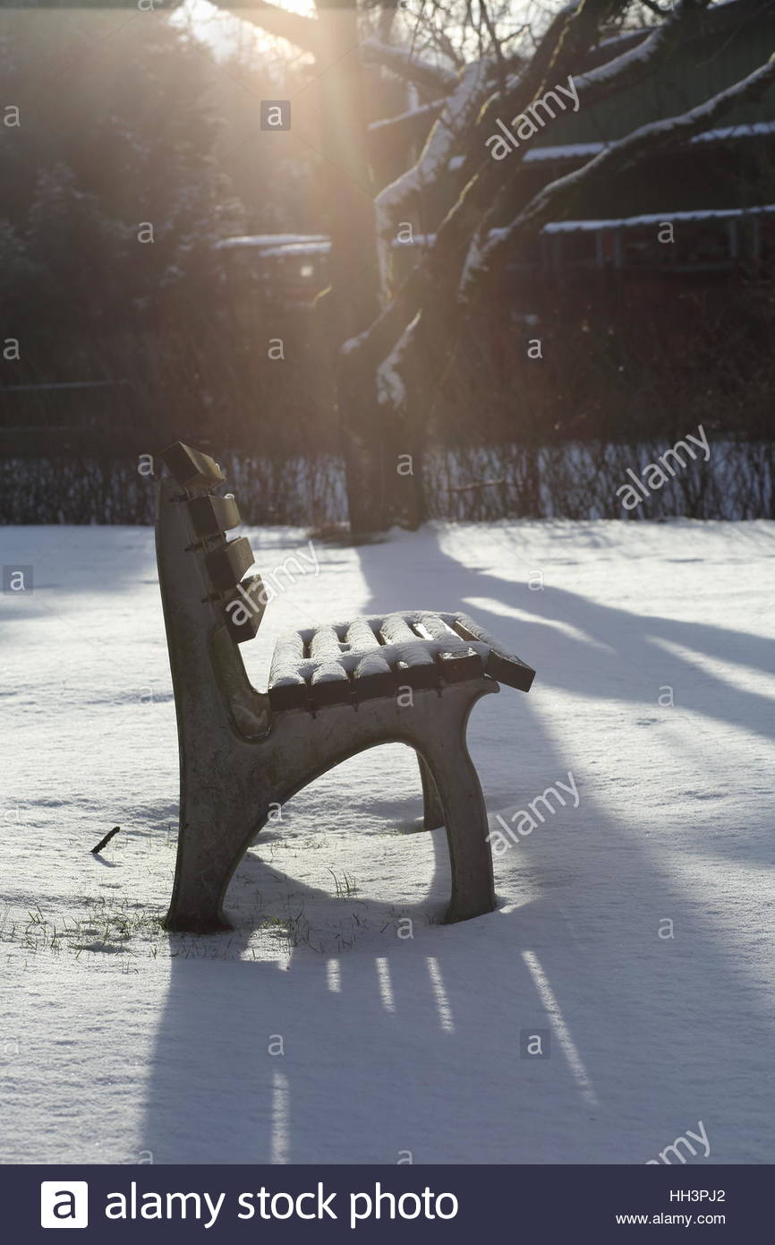 A bench in winter snow in a garden in Bavaria Germany while the sun ...