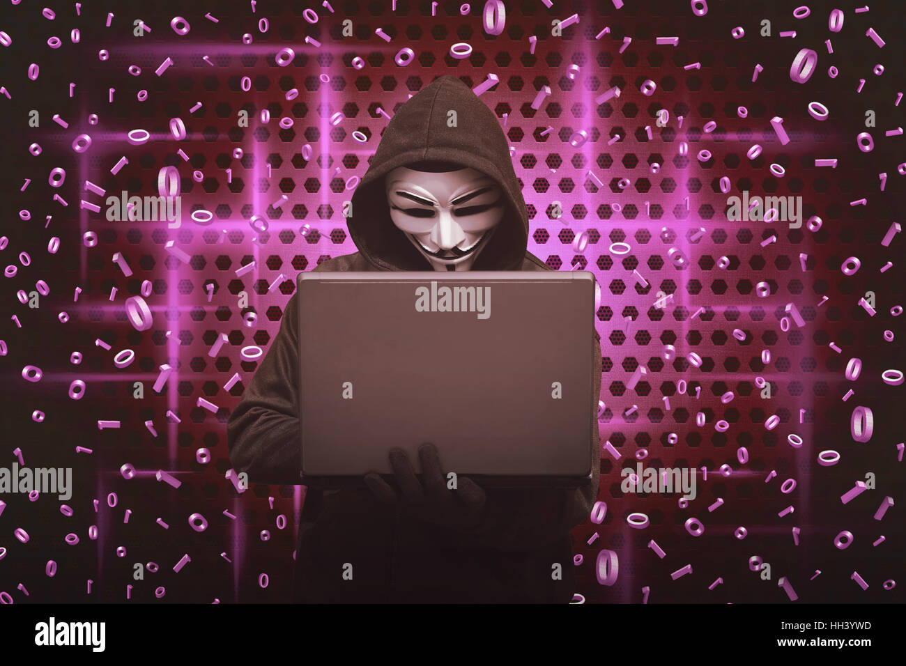 Hooded man wearing mask typing on laptop with binary code in background ...