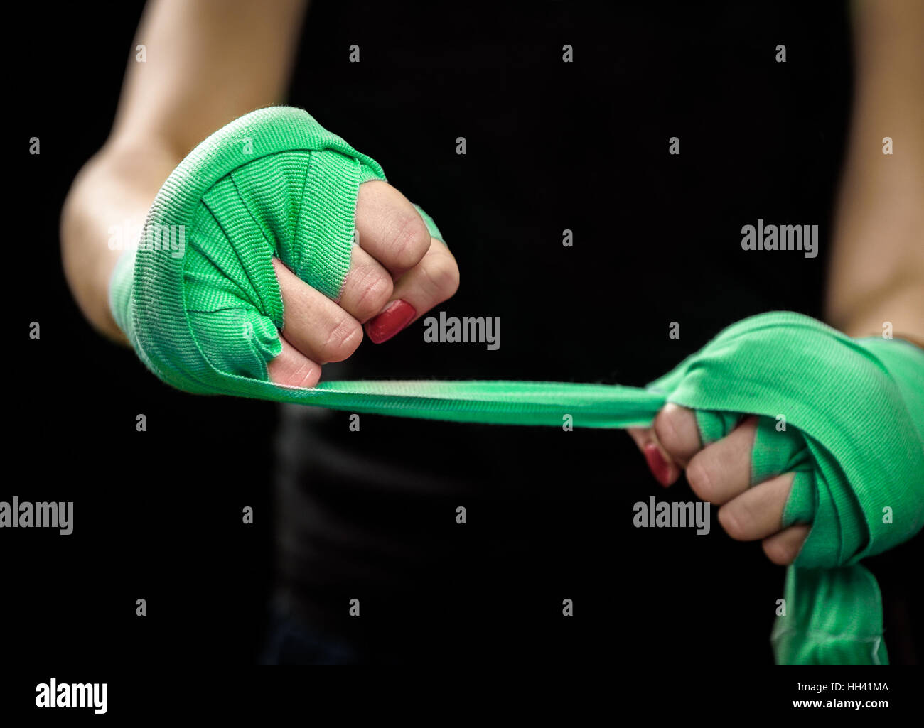 Woman is wrapping hands with green boxing wraps. Isolated on black with ...